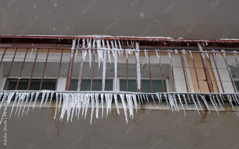 Sharp icicles hanging down in row on balcony of residential building ...