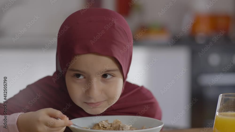 Breakfast in the kitchen. Portrait of muslim girl in hijab eating ...