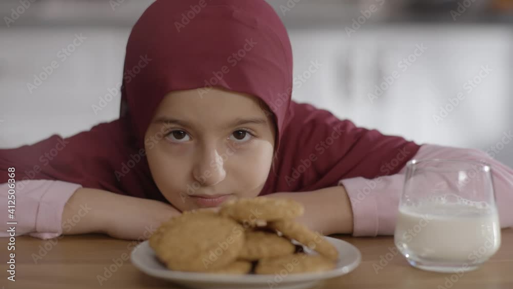 The little Muslim girl wearing a headscarf eagerly looks at the cookies ...