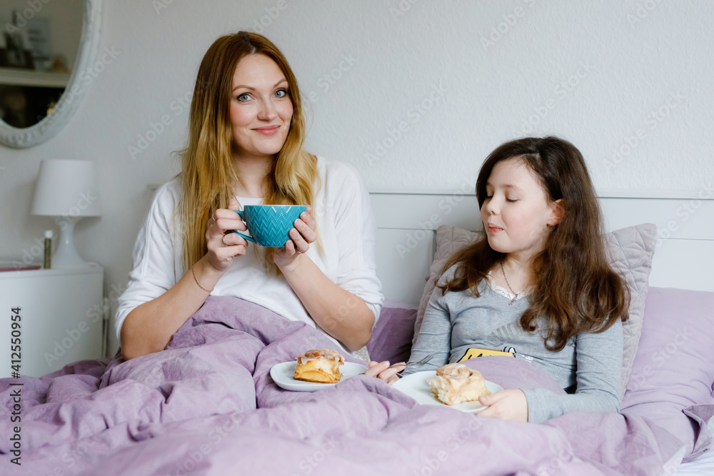 Lovely young mother and cute school kid girl cuddling together in bed ...