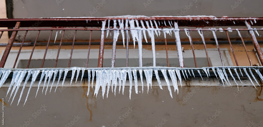 Sharp icicles hanging down in row on balcony of residential building ...