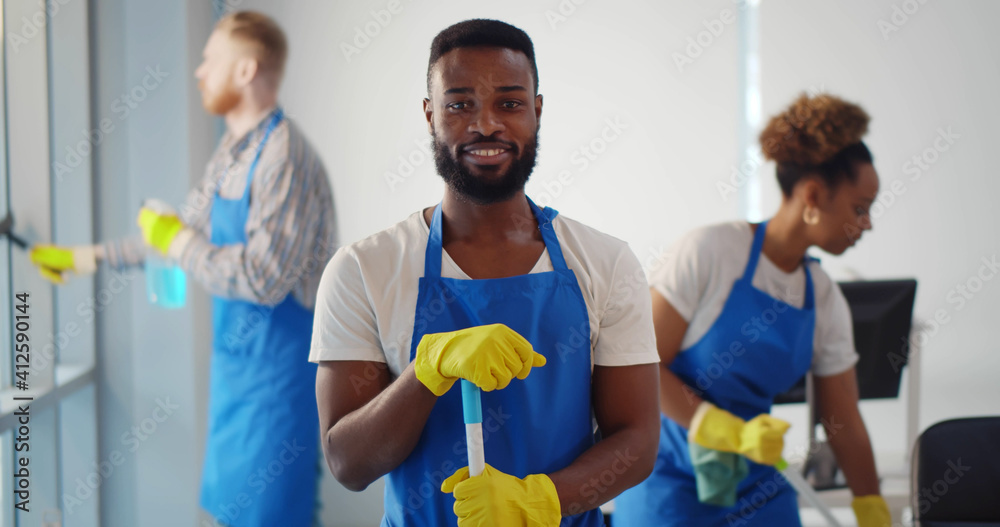 Portrait of african cleaner in apron and gloves holding mop and smiling ...