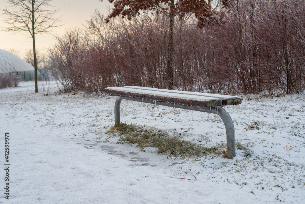 Wooden bench on a metal frame. There is snow and icicles on the bench ...
