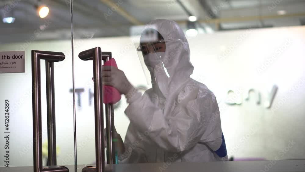 worker wearing ppe suit using alcohol sanitizer spray to clean the door ...