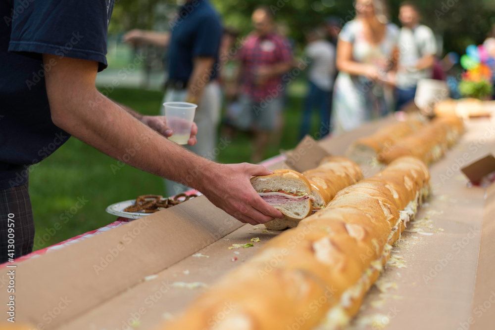 Person grabbing a piece of a sandwich from a buffet line at an outdoor ...