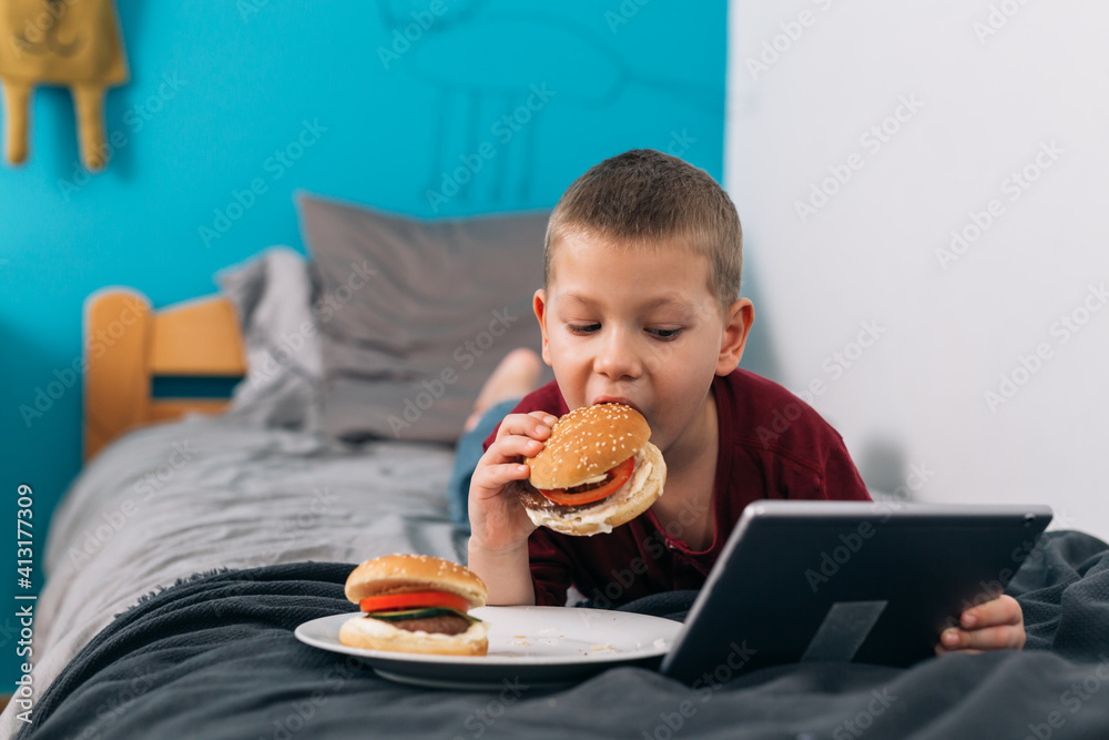 little boy using laptop and eating junk food while laying on bed in his ...