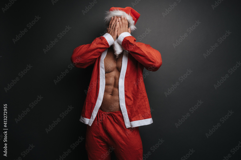 Shirtless muscular man in Santa Claus costume in studio. Emotional ...