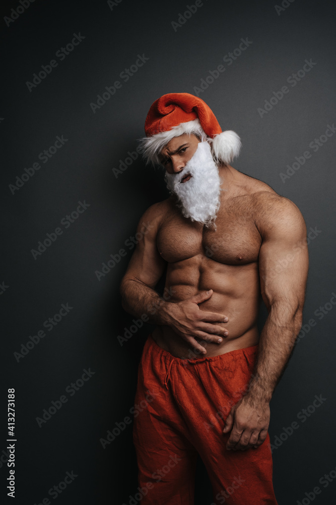 Shirtless muscular man in Santa hat with holding his right hand on his ...