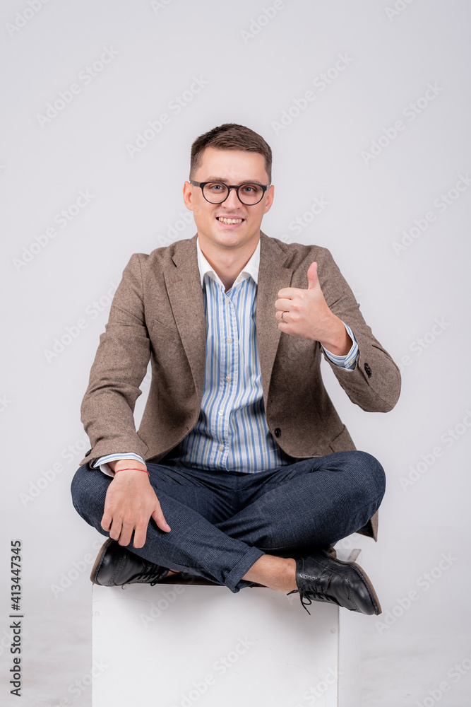 Formal young man sitting cross legged showing thumbs up with one hand ...