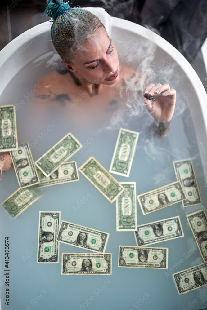 A young sexy tattooed girl enjoying a cigar while having a bath in the ...