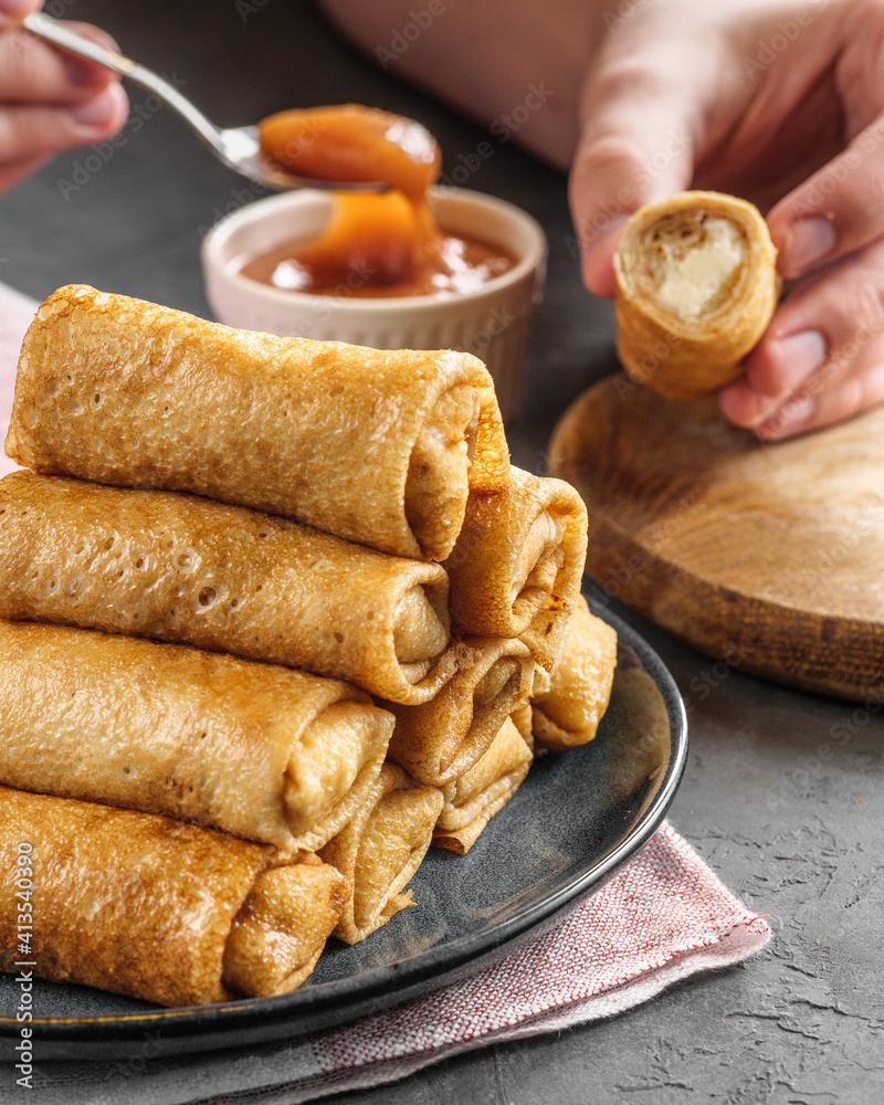 Thin crepe pancakes stuffed lie in a pyramid on the table in a rustic ...
