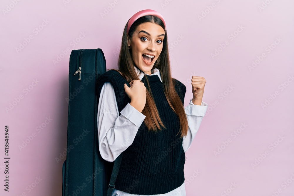 Beautiful brunette young musician woman wearing guitar case pointing ...
