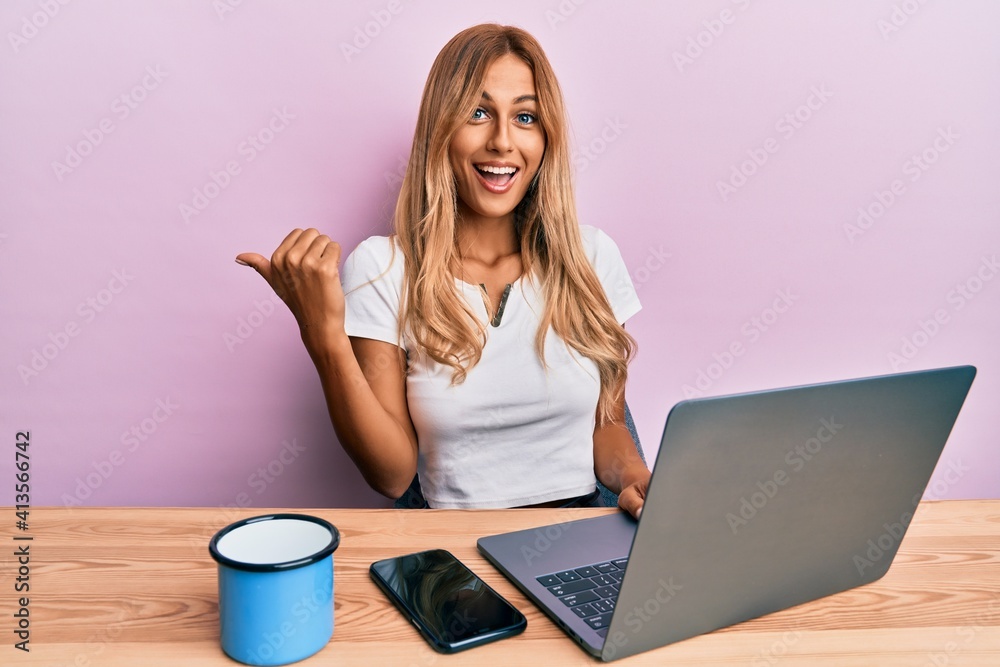 Beautiful blonde young woman working using computer laptop pointing ...