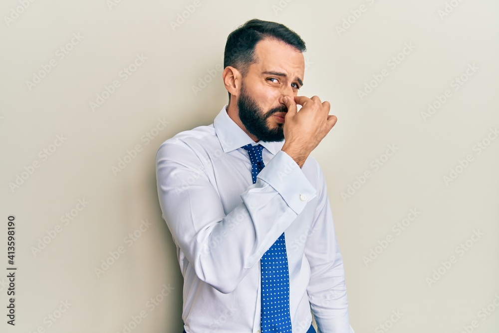 Young man with beard wearing business tie smelling something stinky and ...