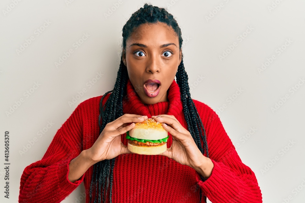 African american woman with braids eating hamburger afraid and shocked ...