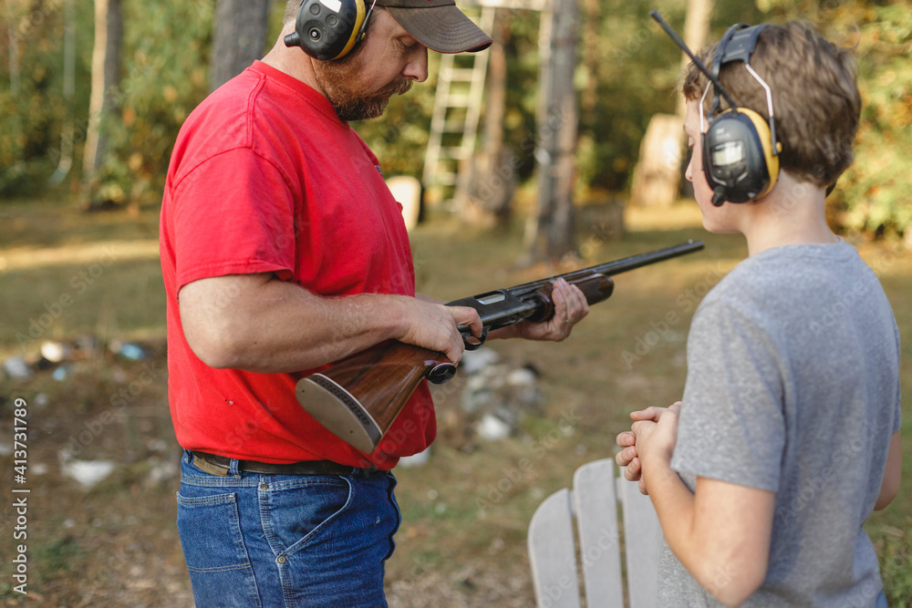 Son wearing headphones while looking at father adjusting rifle in ...