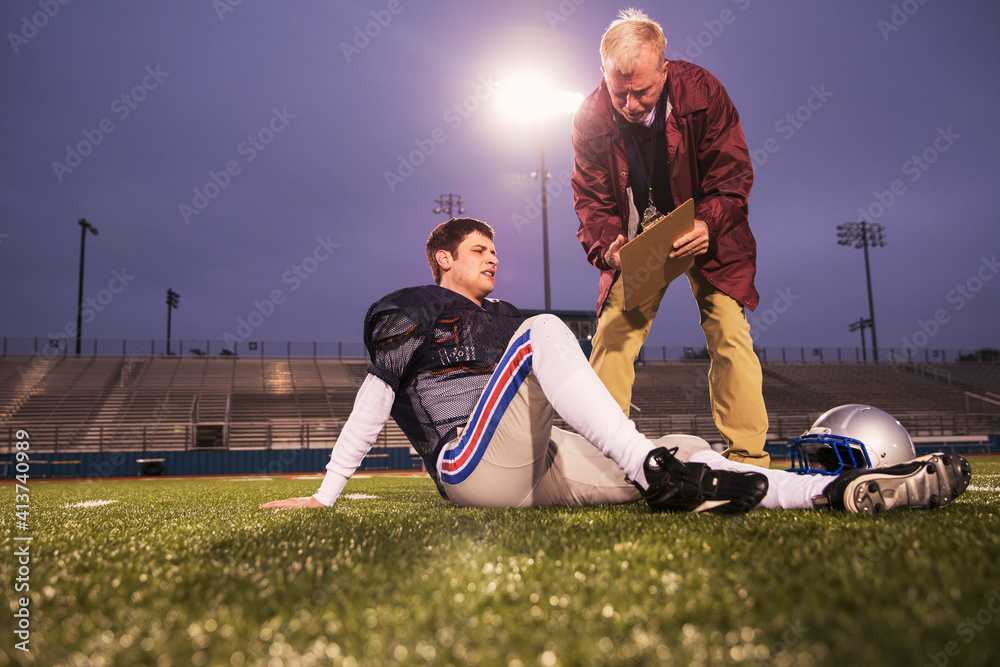 Coach showing clipboard to tired American football player relaxing on ...