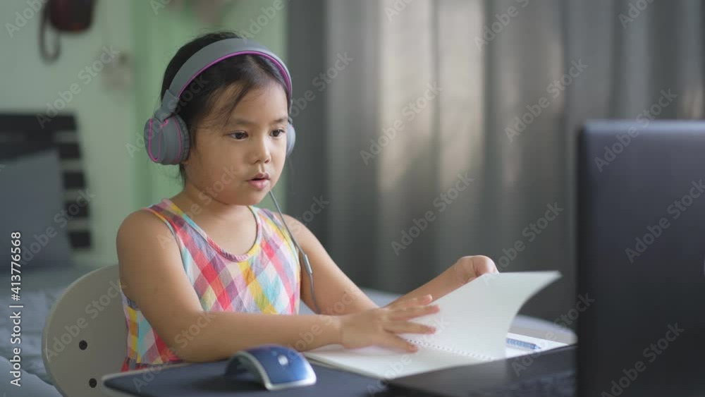 Asian child student or kid girl smile e-learning on computer notebook with wearing headphone and ...