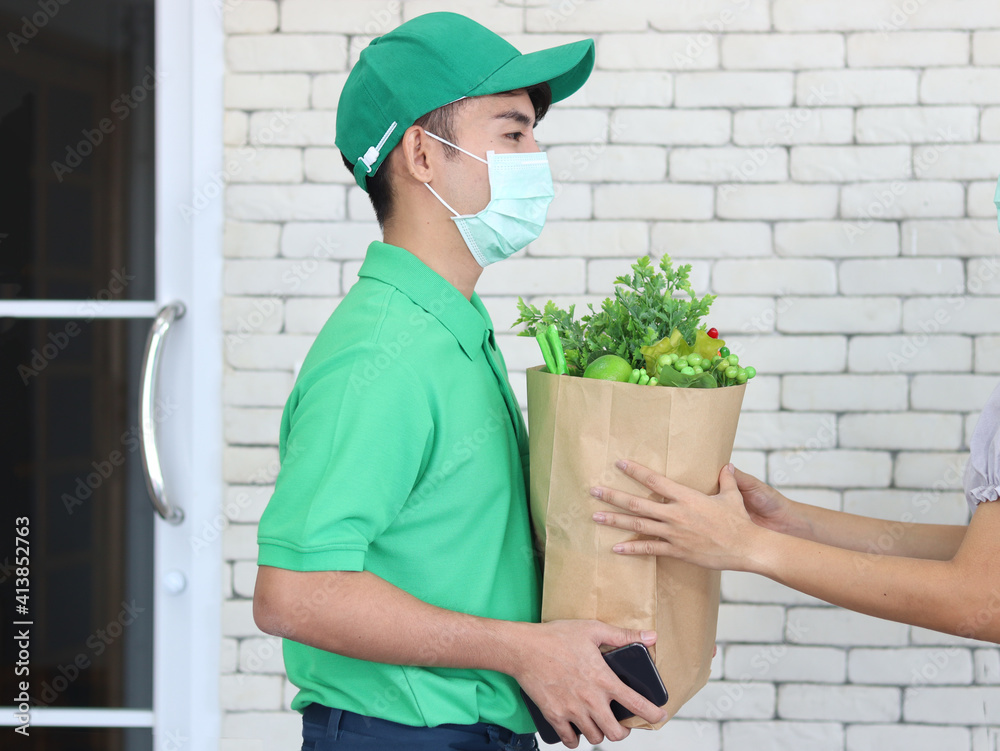 Young Asian delivery man in green T-shirt uniform and cap wearing face ...