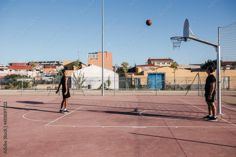 Teenage boy throwing ball into basketball hoop while coach standing at ...