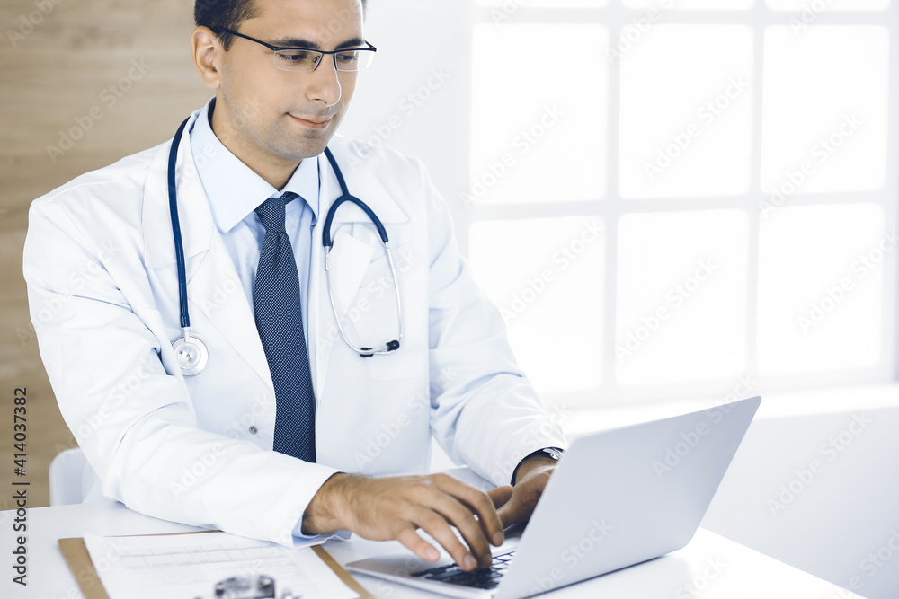 Man doctor typing at laptop computer while sitting at the desk in ...