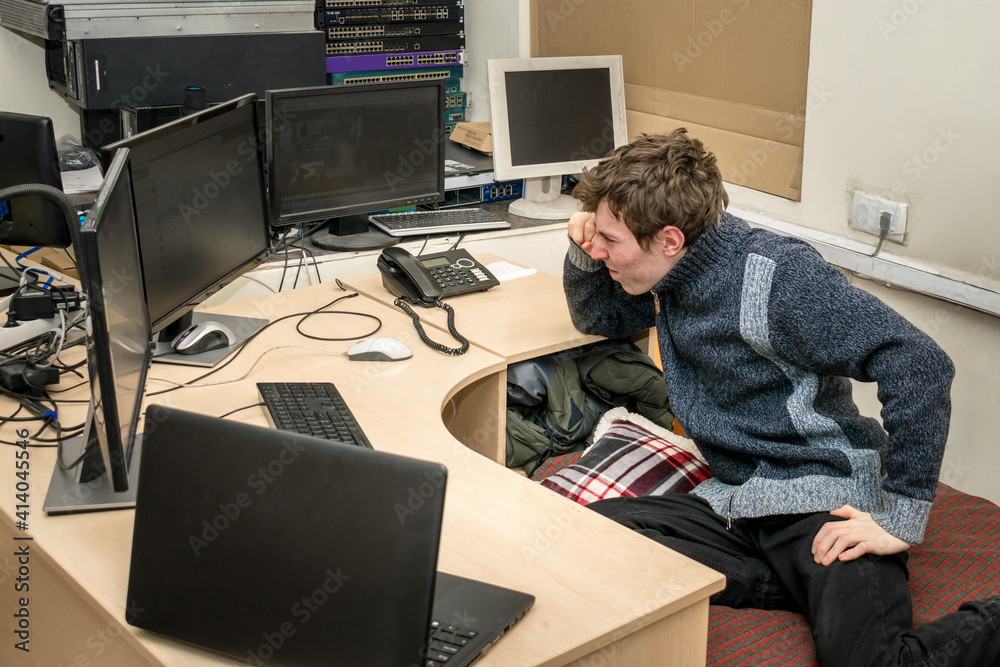 The young man woke up and rubs his eyes in front of the monitor screens ...