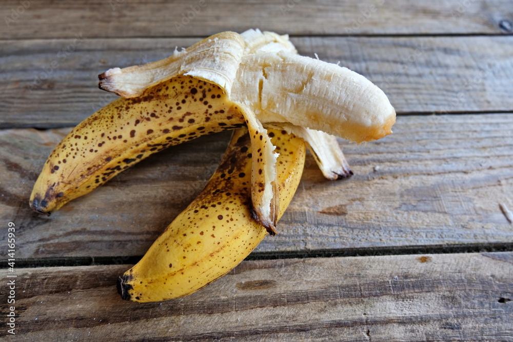 Overripe bananas with dark spots on the skin. One peeled banana and one ...