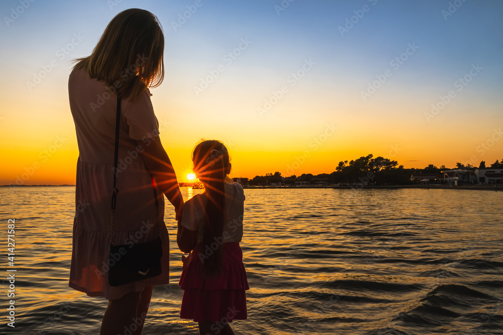 Mother and daughter holding hands, admiring beautiful sunset at ...