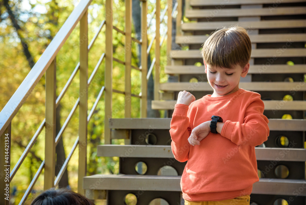 A cute boy wearing stylish shirt stay near school, looking at his smart ...