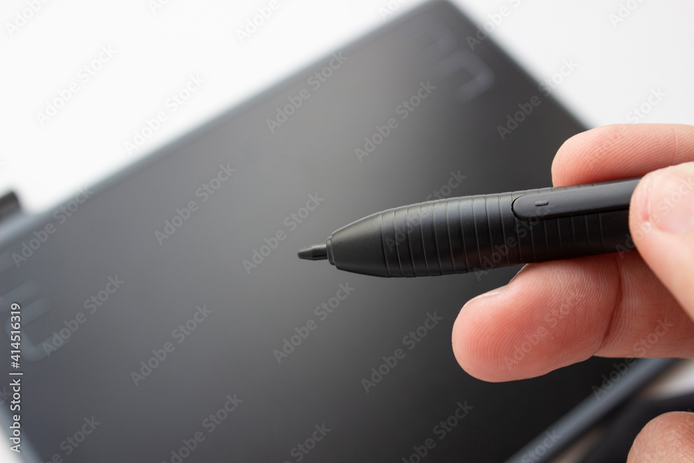 A person draws on a graphics tablet. The hand holds the touch pen ...