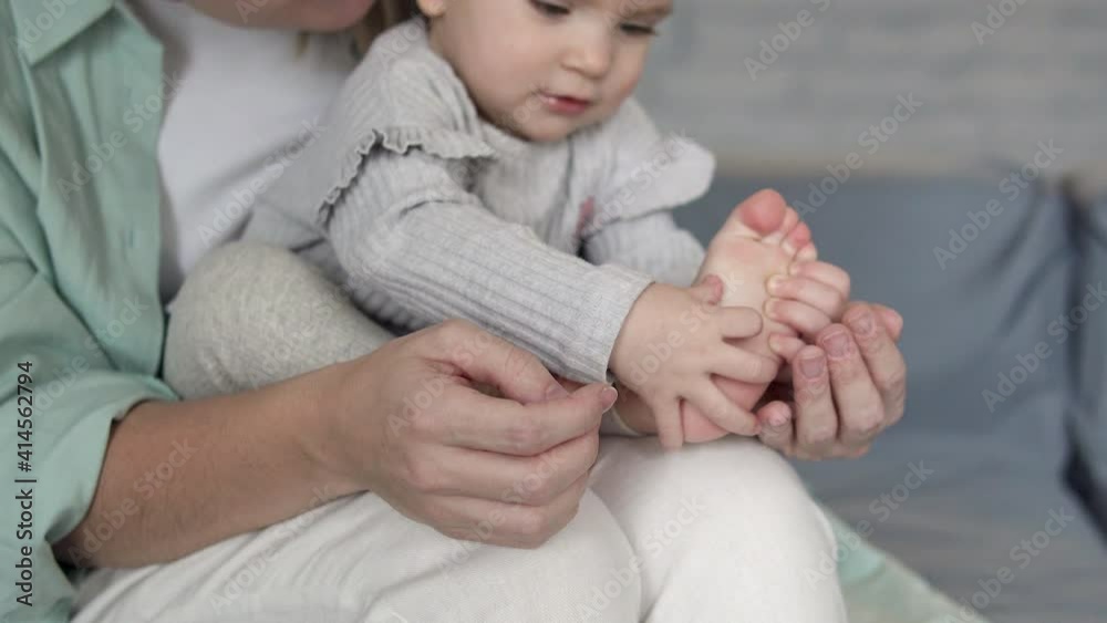 Cute child exploring her leg touching toes and heel, smiling when mommy ...
