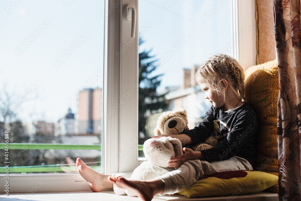 Cute little girl enjoying the sunshine while sitting at the window. The ...
