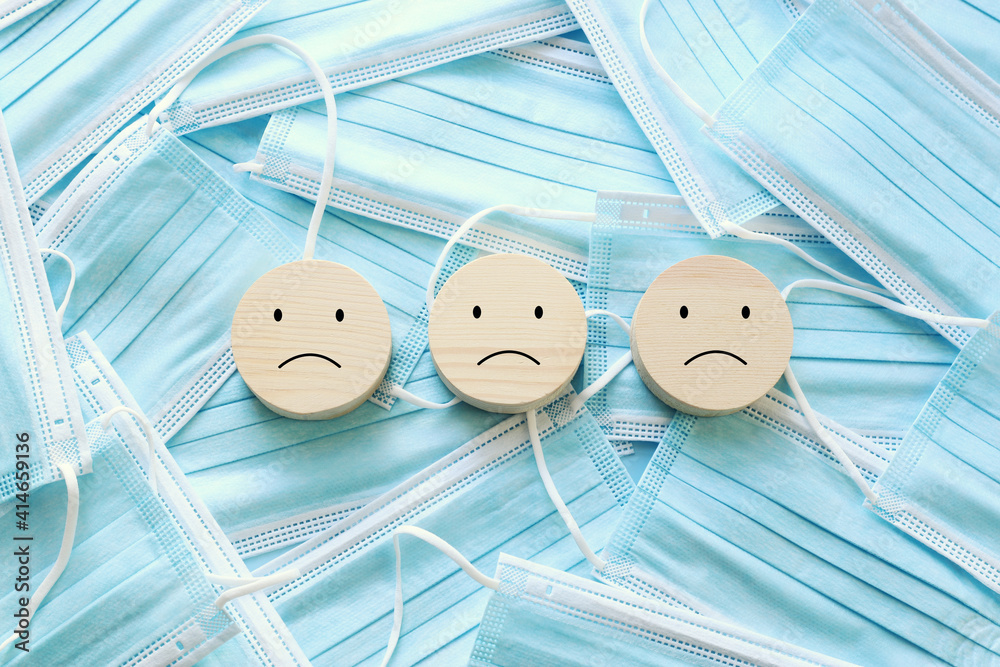 wooden cube with sad face over protective face masks pattern. concept ...