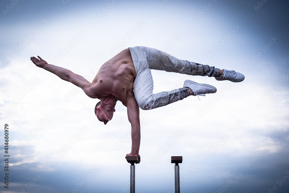 Circus artist keeps balance on one hand on the cloudy sky background ...