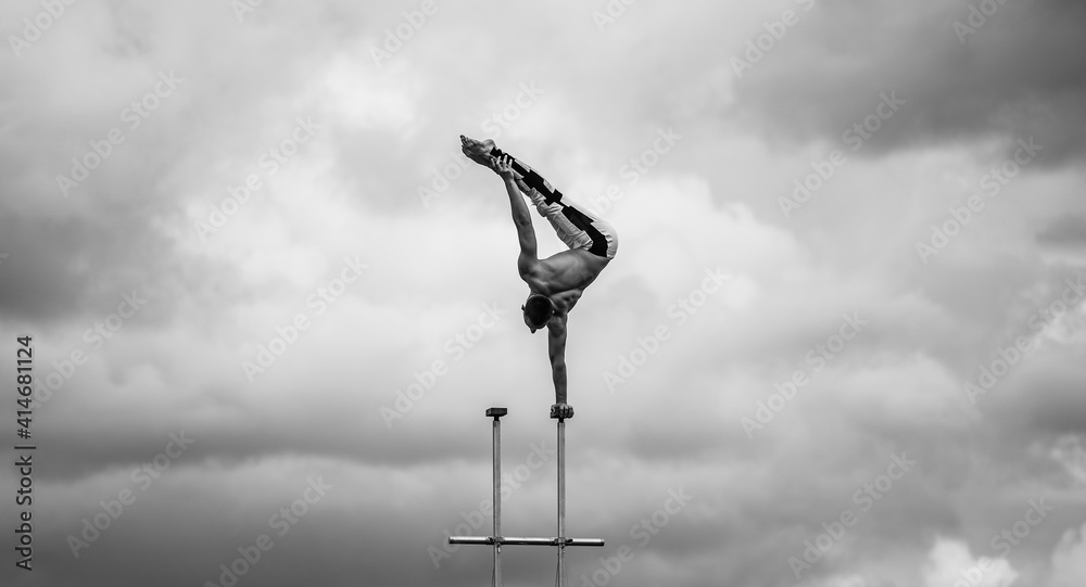 Man keeps balance on one hand on the cloudy sky background. Concept of ...