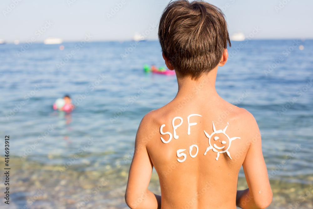 Child, preteen boy with sun protection cream on his back on the beach ...