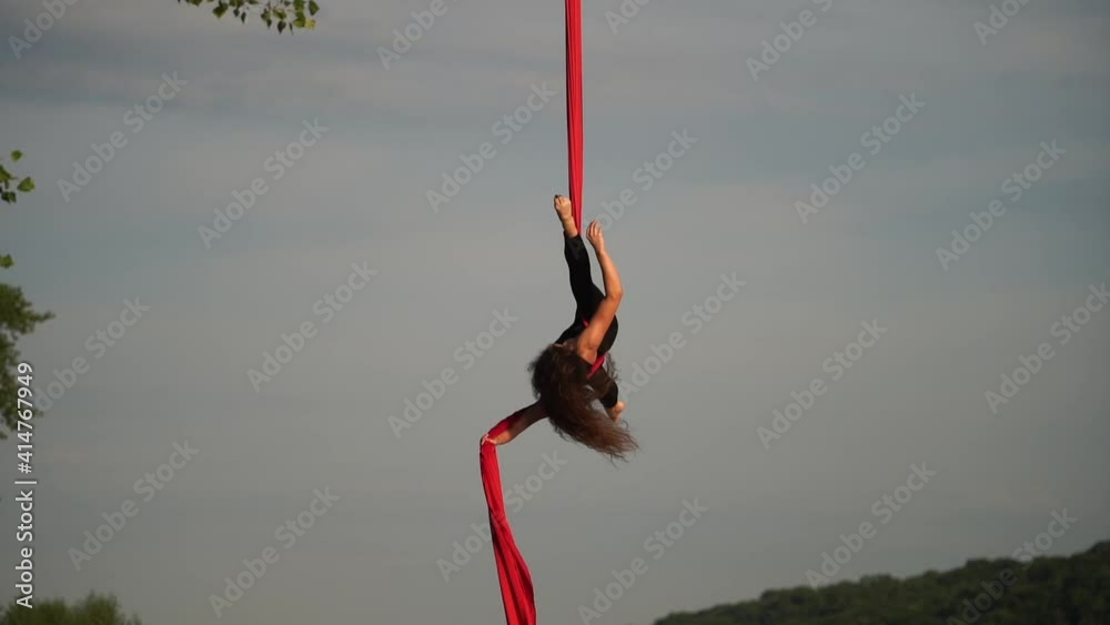 Female acrobat showing her flexibility and splits with red aerial silk ...
