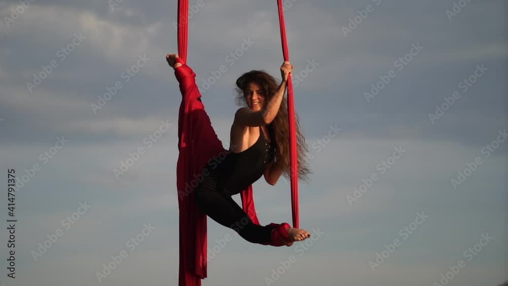 Female acrobat showing her flexibility and splits with red aerial silk ...