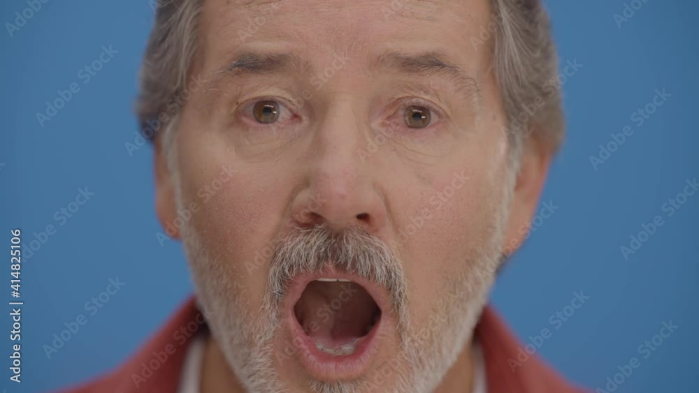 In front of the blue background, bearded old man is shocked. Face plan ...