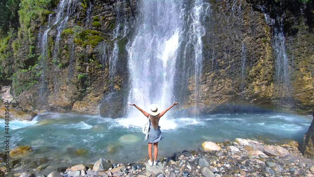 Woman in blue swimsuit and hat rises her arms while she looks at huge ...