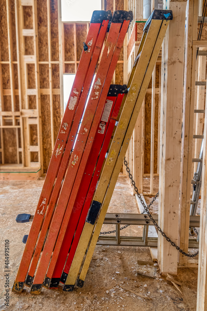 Red, orange, yellow tall aluminum construction ladders leaning on each ...
