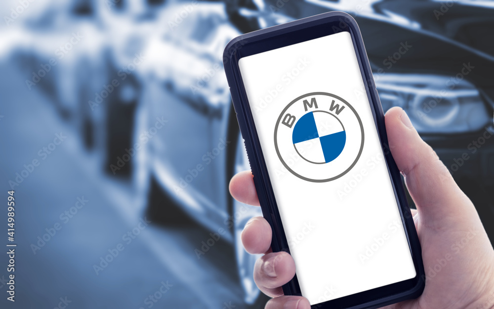 Hand holding a smart phone with new BMW logo on screen and blurry cars ...