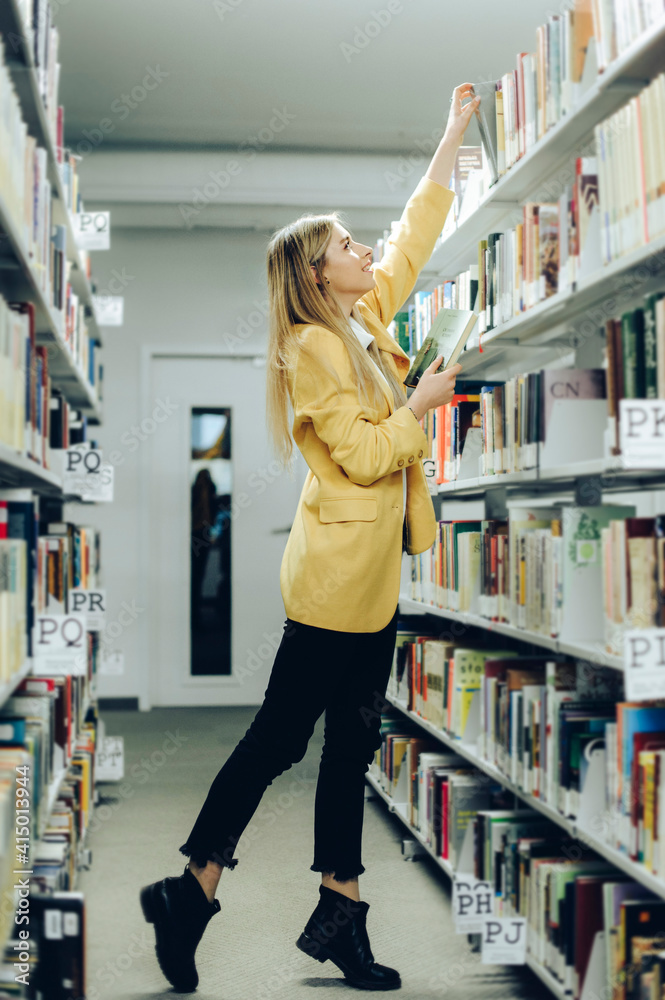 Beautiful girl student reads books in a library on the window sill ...