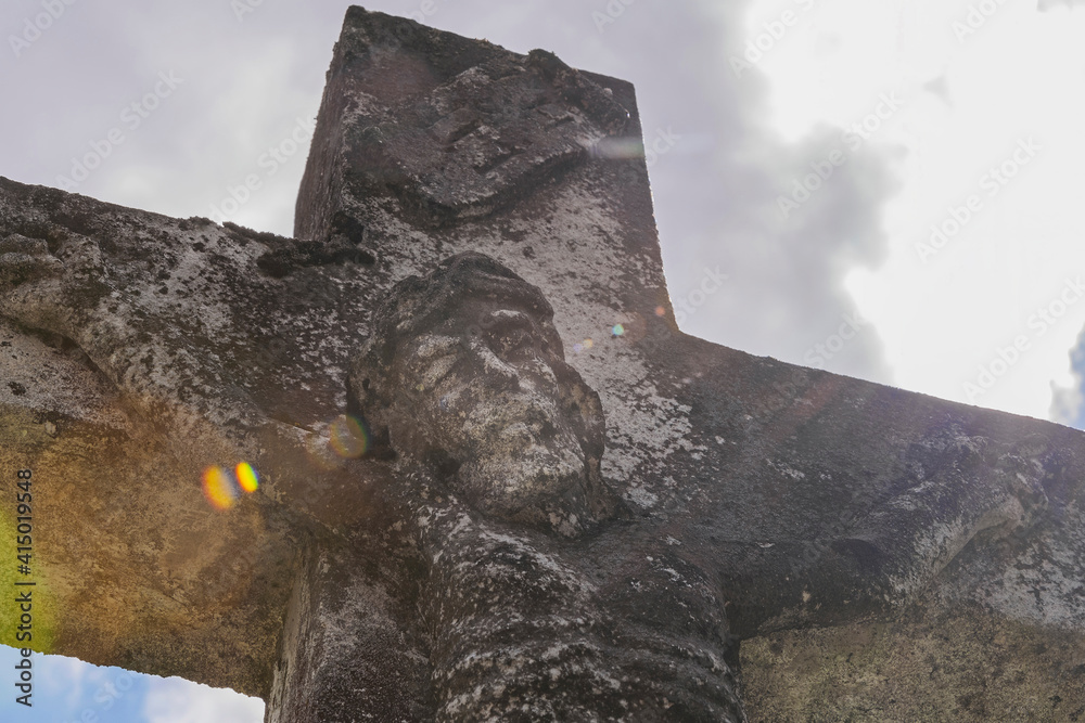 Ancient stone sculpture of Jesus Christ, crucified on a cross. The sun ...
