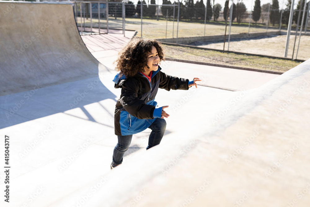 Side view of positive ethnic child with Afro hairstyle running up ramp ...