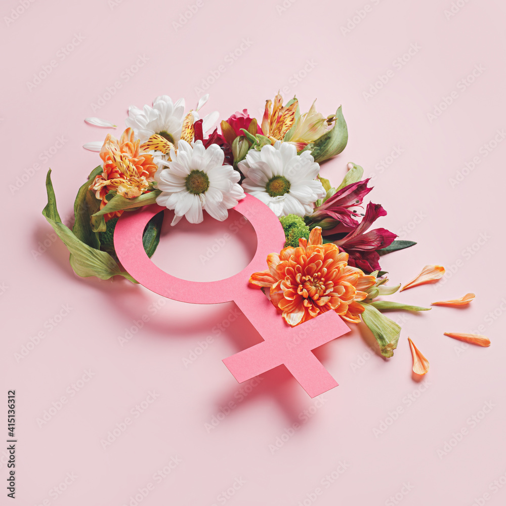 Female symbol with fresh spring flowers and leaves against pastel pink ...