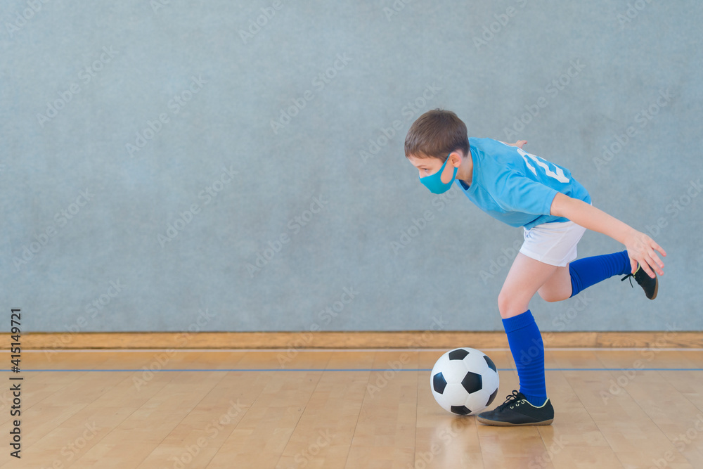 School kid with mask and soccer ball in a physical education lesson ...