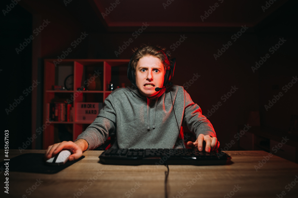 Emotional gamer guy playing computer games at home at night in a room ...