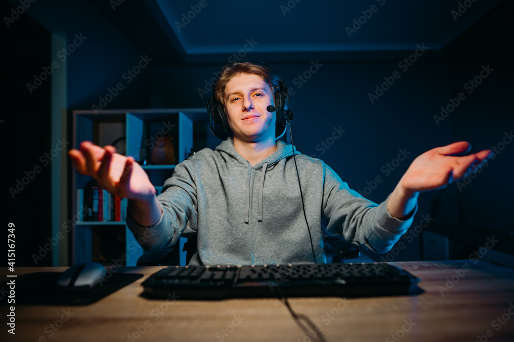 Foto de Positive young male gamer in a headset on his head spreads his ...