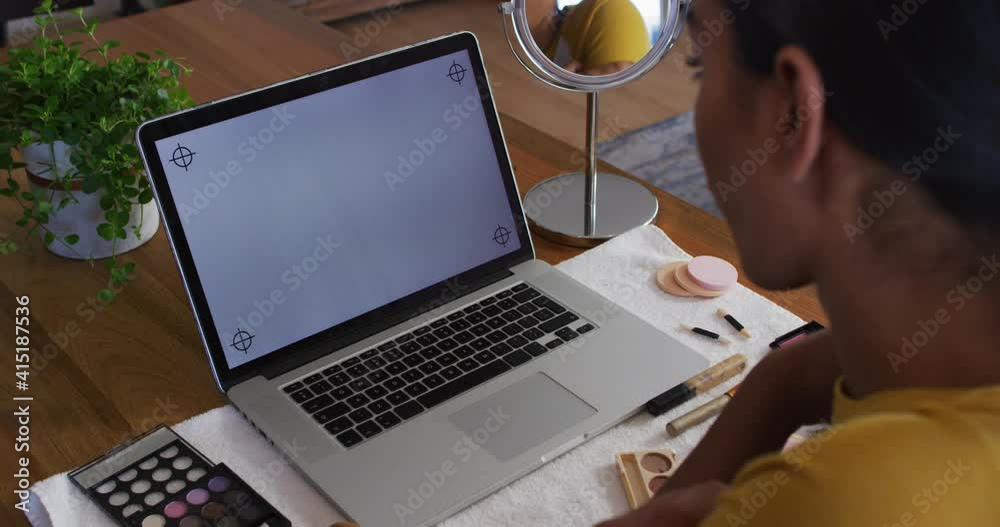 Mixed race gender fluid person sitting by desk and using laptop at home ...